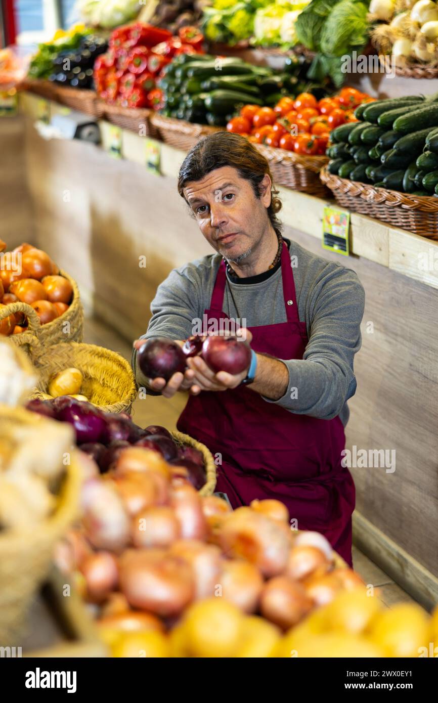 Male grocery store worker arranges red onion and other vegetables on ...