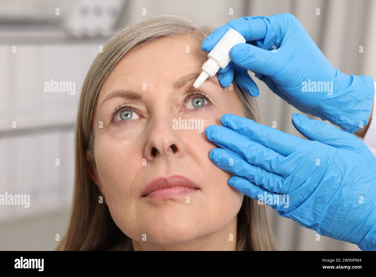 Medical drops. Doctor dripping medication into woman's eye indoors ...