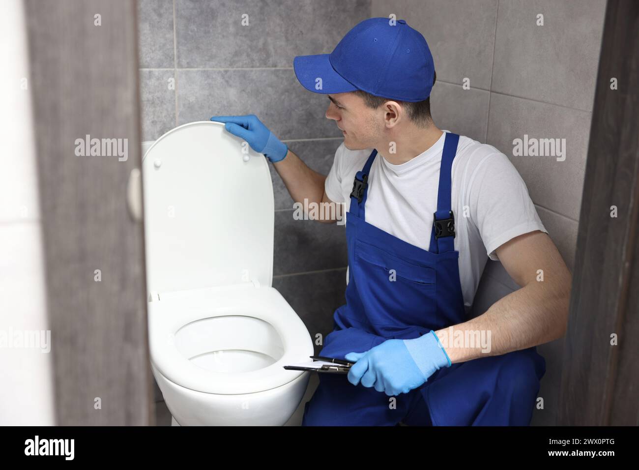 Plumber examining toilet bowl in water closet Stock Photo - Alamy