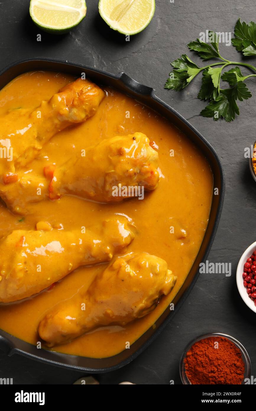 Tasty chicken curry and ingredients on black textured table, flat lay ...
