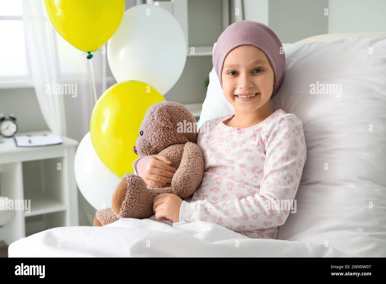 Little girl after chemotherapy with toy bear lying in bed at hospital ...