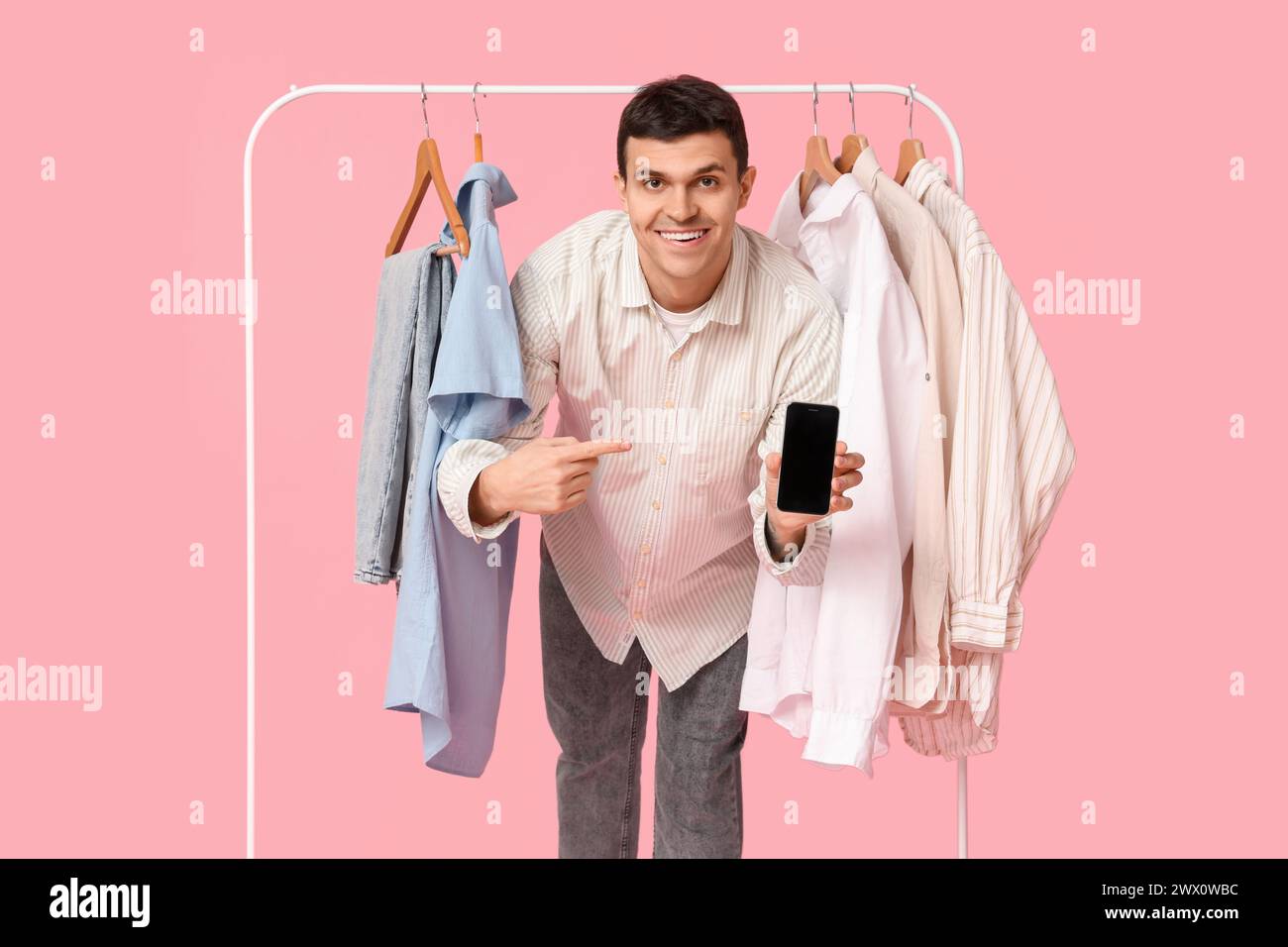 Handsome Young Happy Man Pointing At Mobile Phone And Rack With Stylish