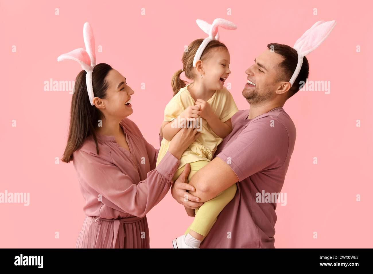 Happy parents in Easter bunny ears tickle their daughter on pink ...