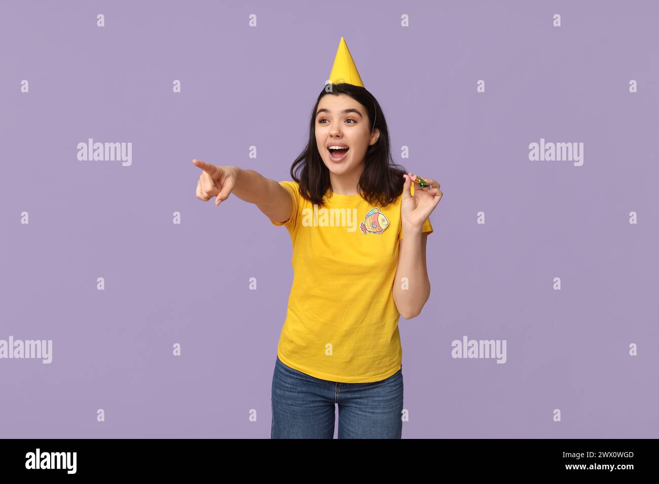 Beautiful young shocked woman with paper fish and whistle pointing at ...