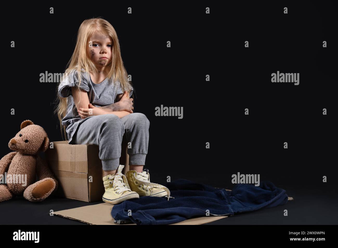 Homeless little girl sitting on cardboard box against dark background ...