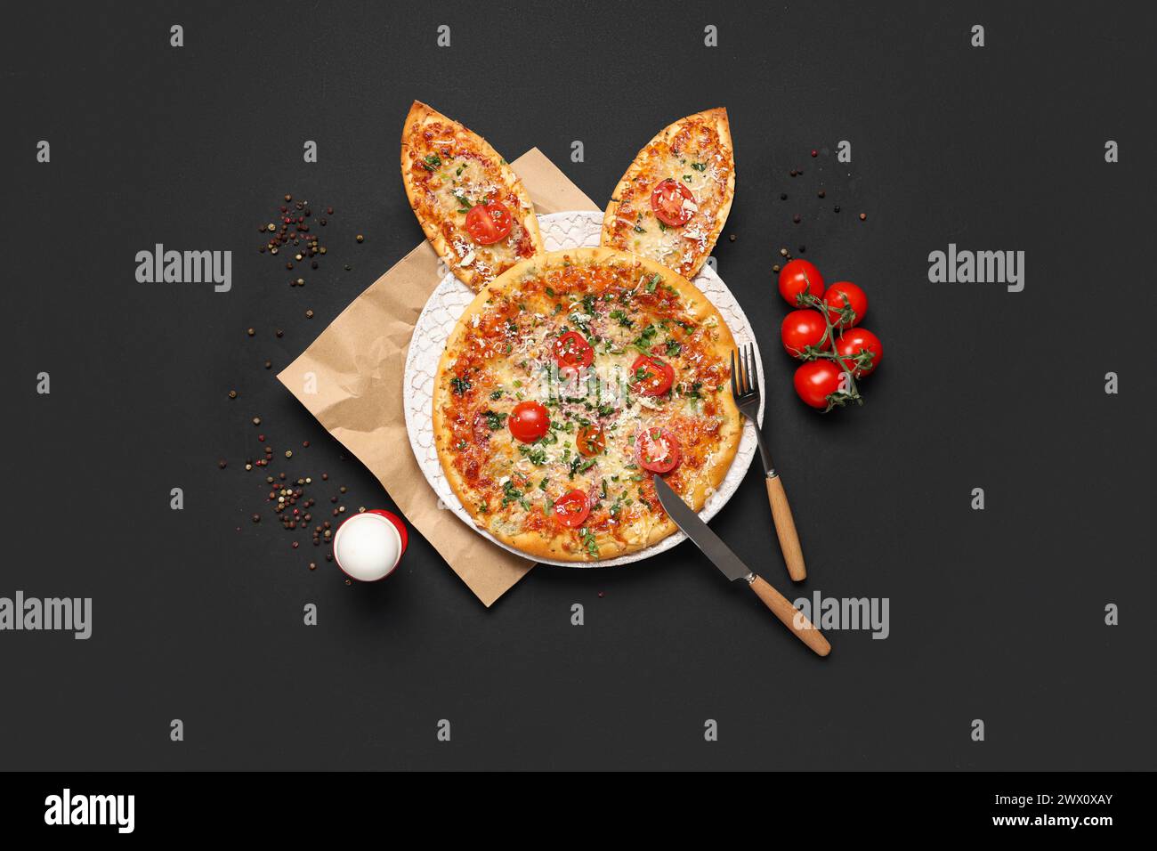 Tasty Easter pizza with bunny ears, egg, tomatoes and cutlery on black ...