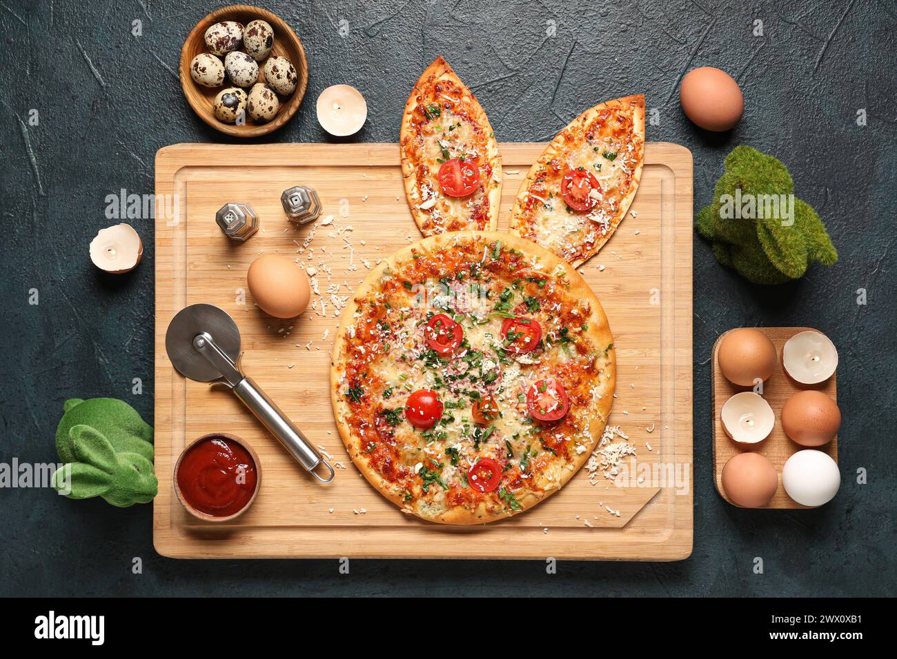 Board of tasty Easter pizza with bunny ears, eggs and sauce on black ...