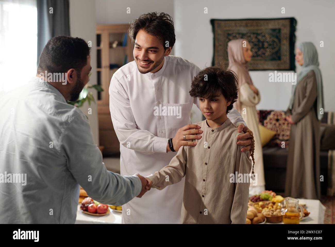 Medium shot of modern Muslim man and his son wearing thobes greeting ...