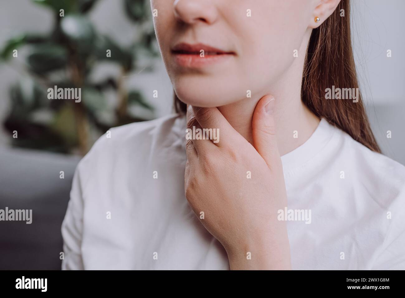 Close up of sad young woman with sore throat sitting alone on couch ...