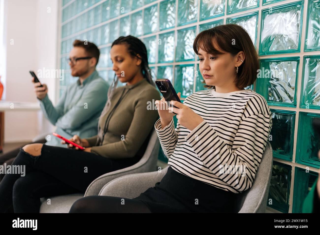 Serious multicultural young business people sitting in row using ...