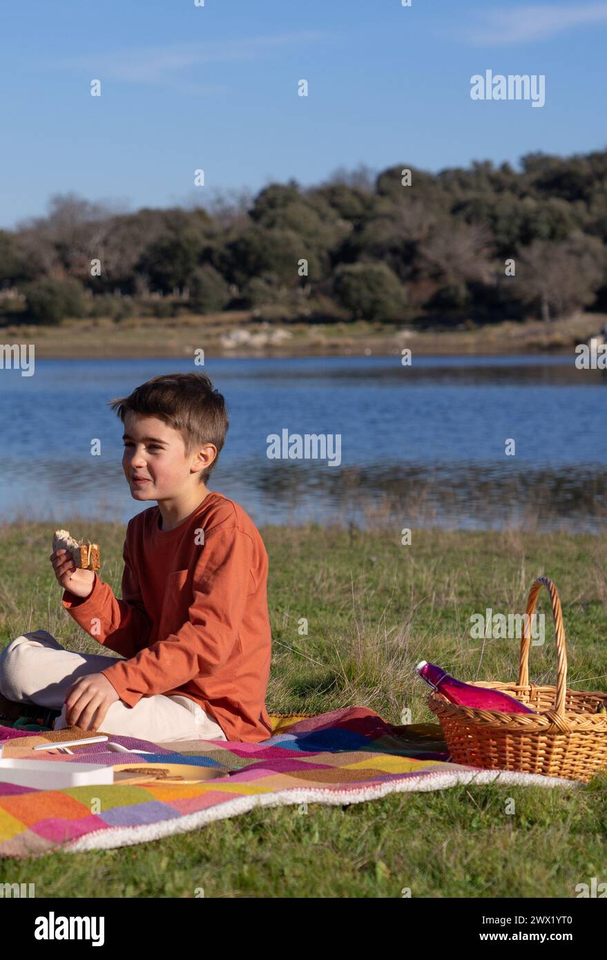Boy eating a sandwich while picnicking at a lake in an orange t-shirt ...