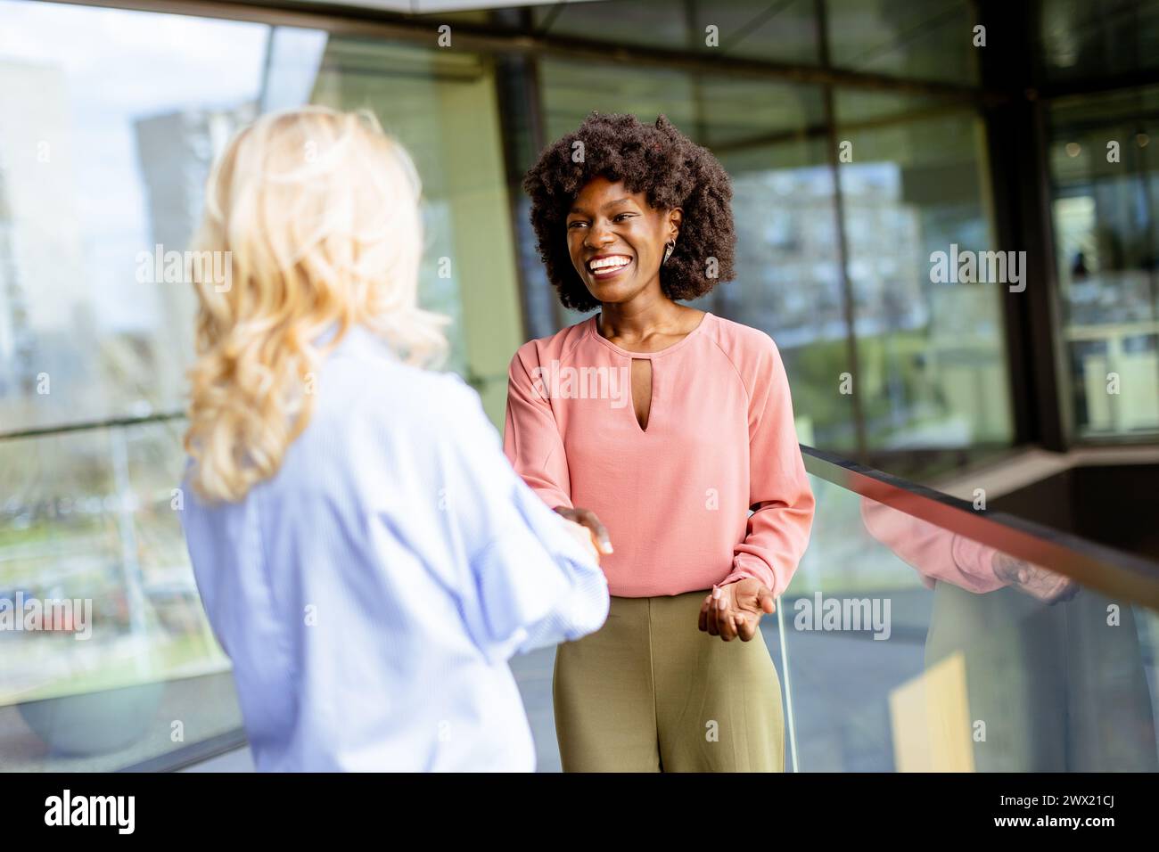 Two women engage in a friendly handshake, one laughing joyously ...