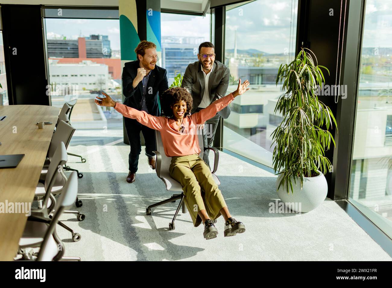 Exuberant co-workers engage in an impromptu office chair race, basking ...