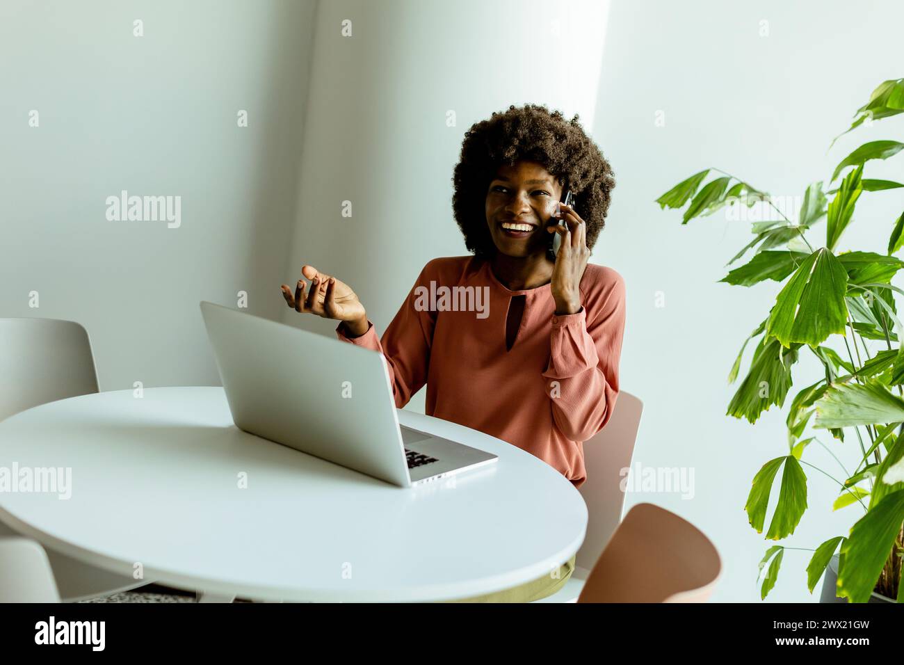 Confident woman multitasks with a phone call and laptop in a bright ...
