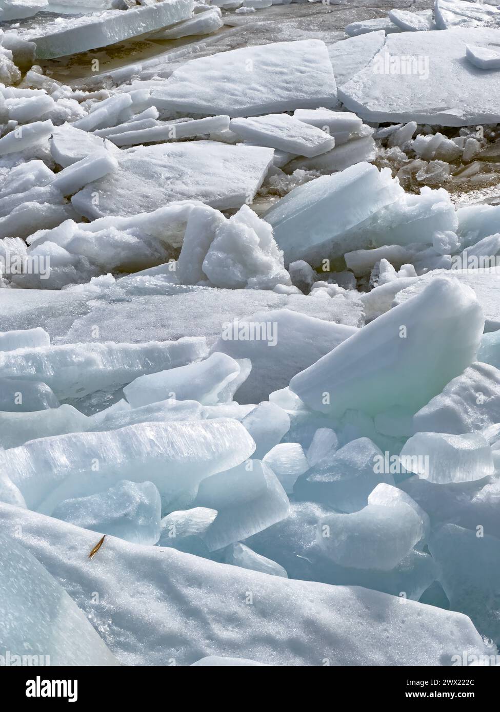 Close-up view of melting ice and snow revealing water and rocks beneath ...