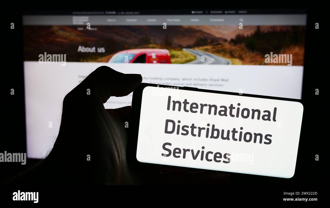 Person holding cellphone with logo of British company International Distributions Services plc ...