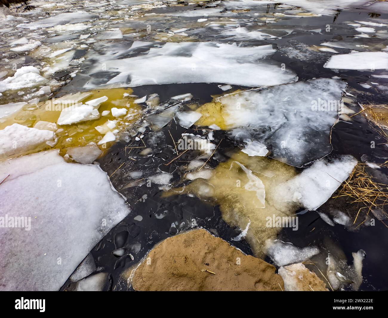 Close-up view of melting ice and snow revealing water and rocks beneath ...