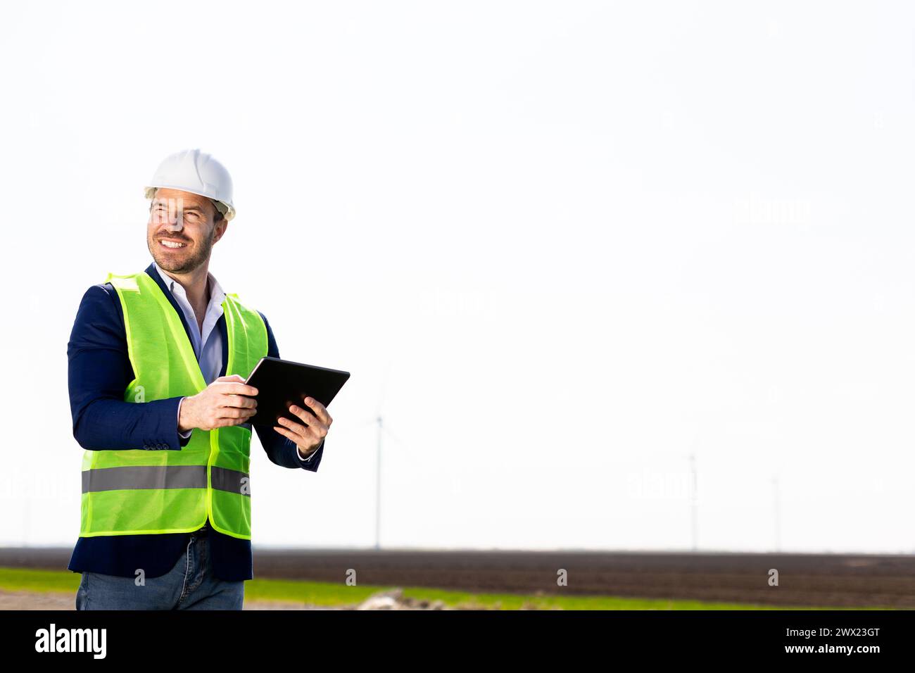 A safety-helmeted engineer with clipboard scrutinizes the workings of a ...