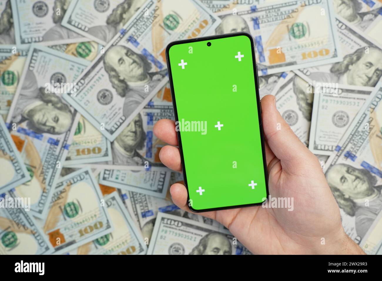 Hand holding smartphone with green screen on pile of dollar banknotes ...