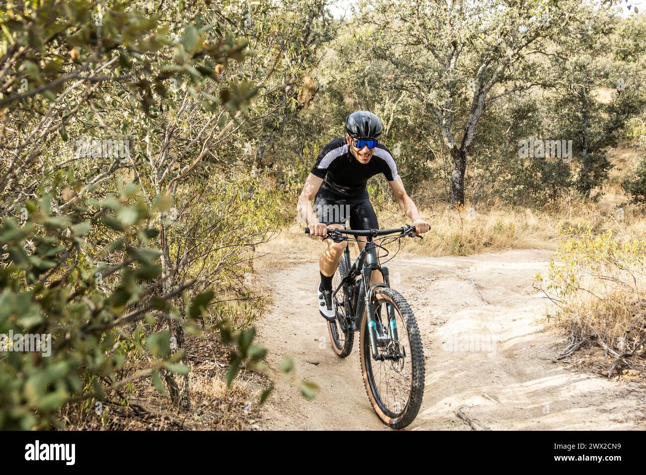 front view of a young adult mountain biker riding up a trail in a ...