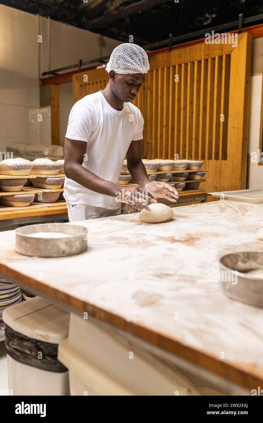 young black male apprentice, kneading bread dough on the bakery school ...