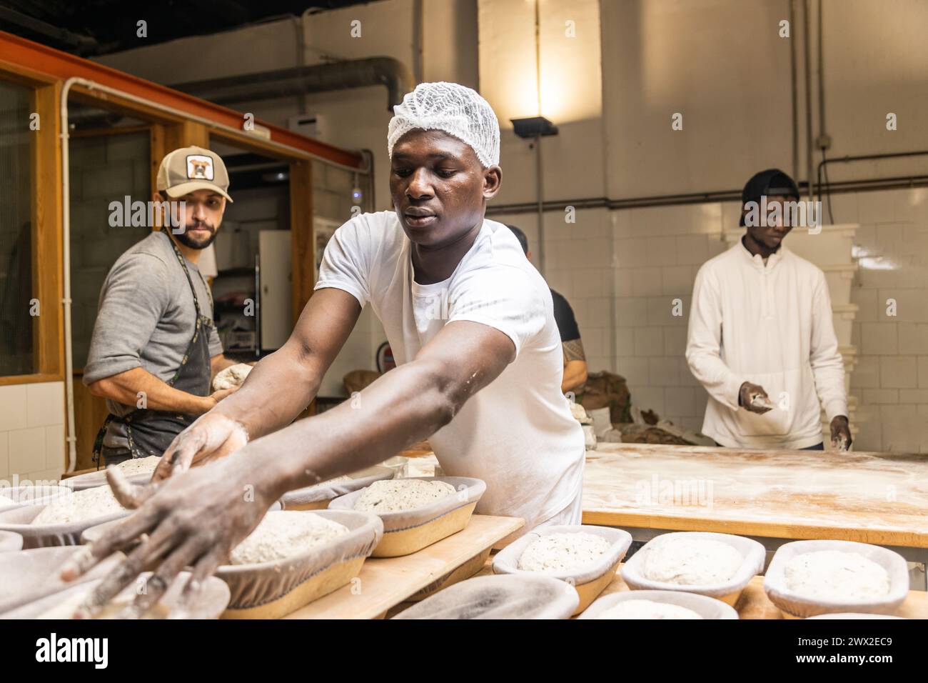 Multi-ethnic group of colleagues working in a bread factory, teaching ...
