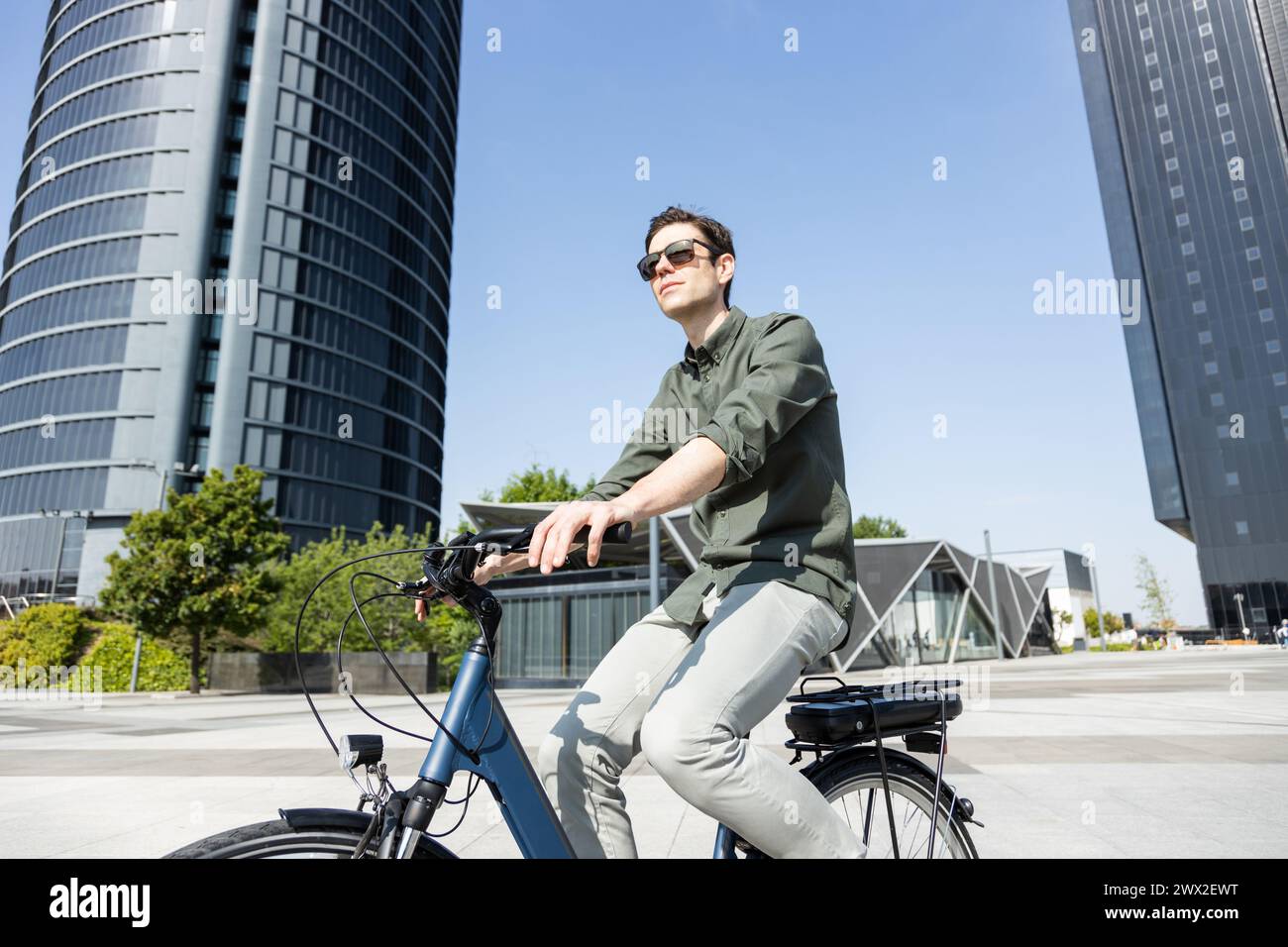 young businessman rides e-bike on his way to the tower where his office ...