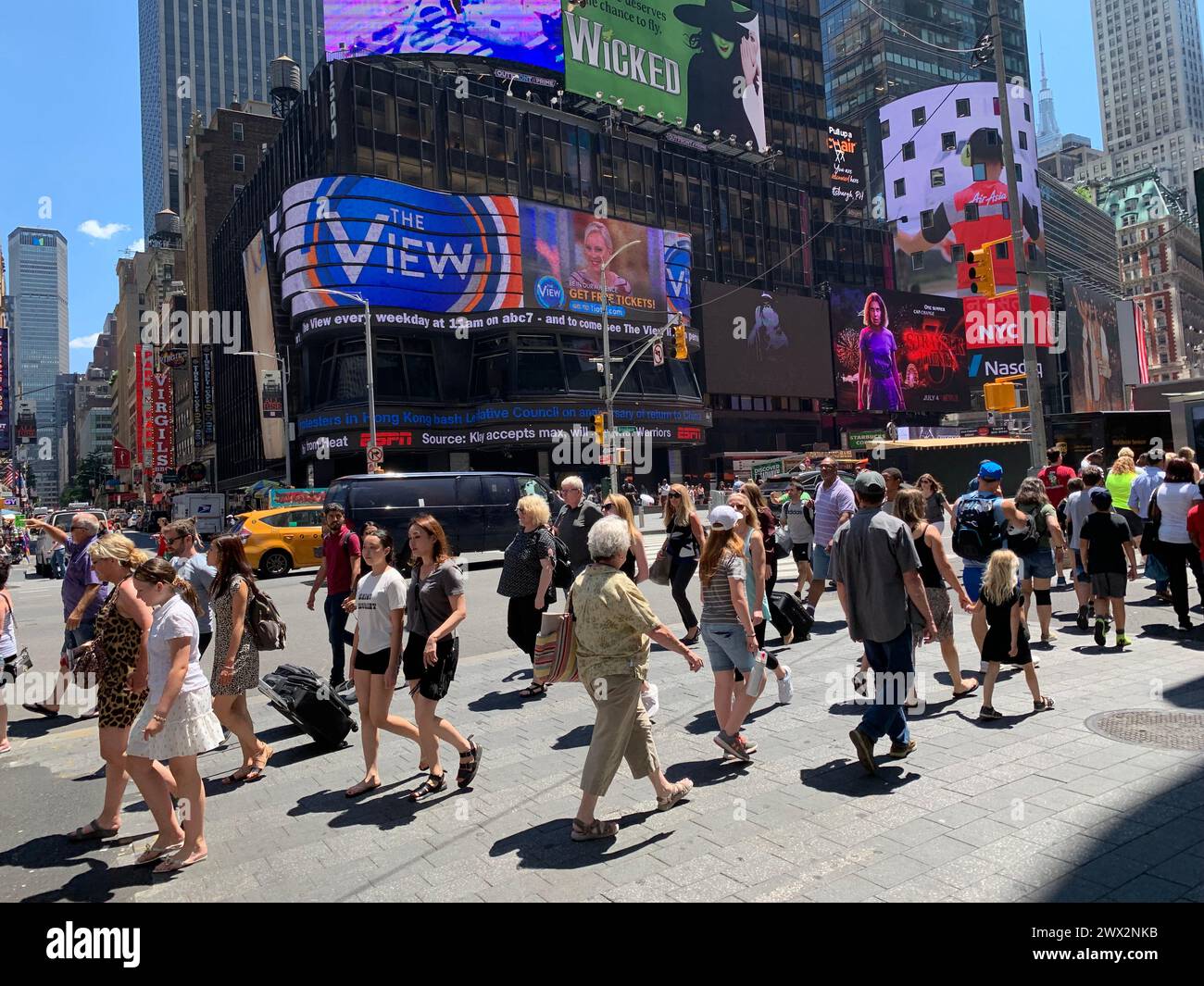 A large crowd of tourists and families walk across the street in New ...