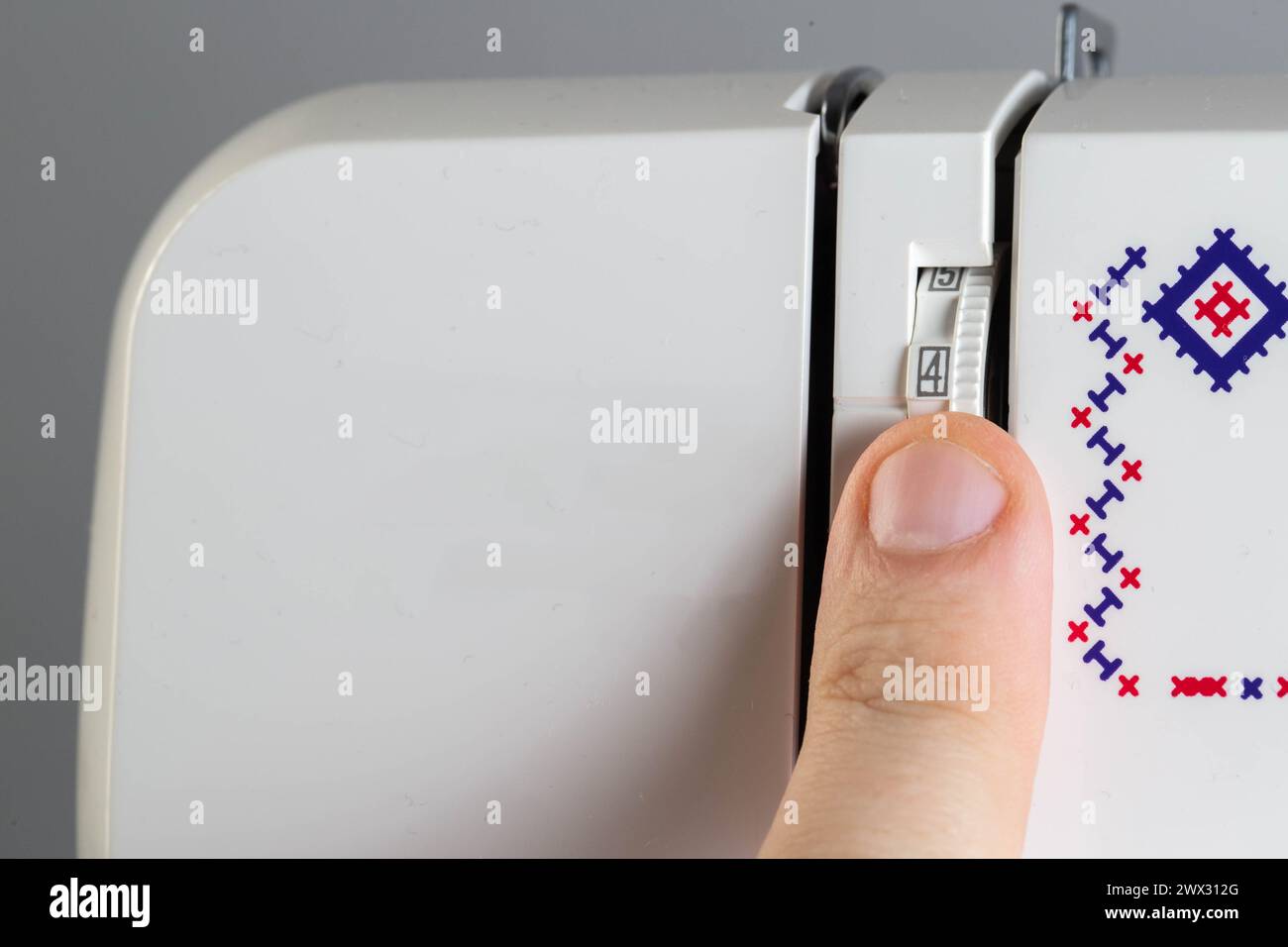 A seamstress's finger adjusts the stitch length dial of a sewing ...