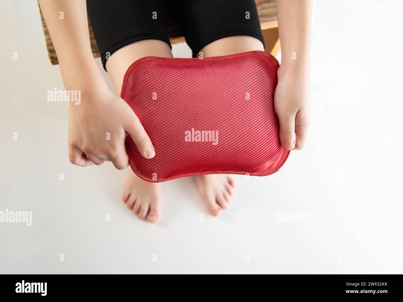A little girl applies a red heating pad with hot water to her knee ...