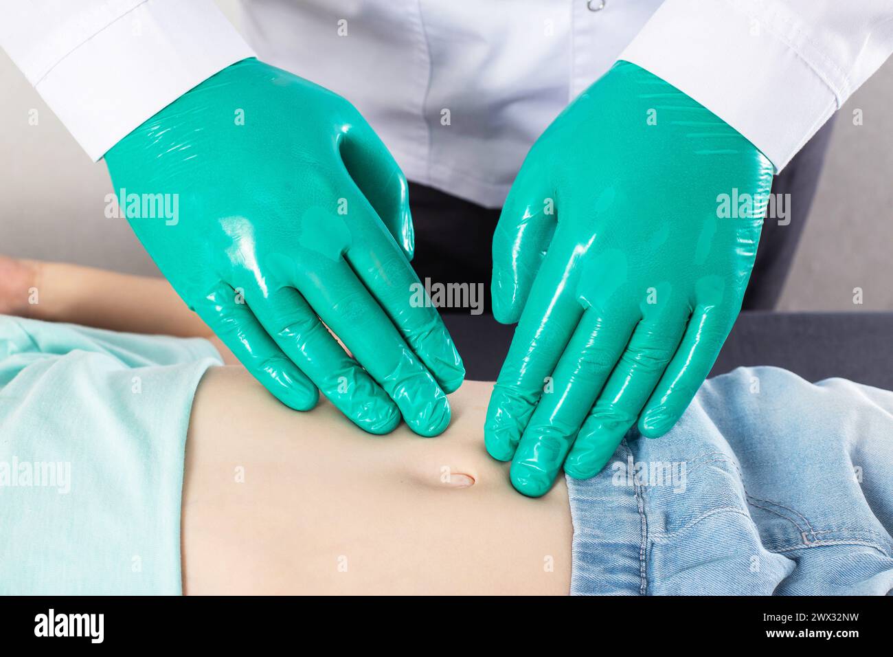 The doctor's hands in green medical gloves probe the child's abdomen in ...