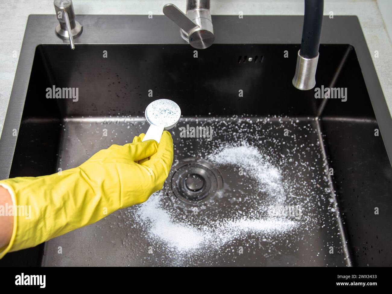 A man's hand in a yellow glove holds a spoon with oxygen bleach against ...