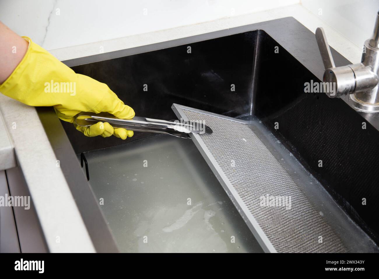 A girl's hand in a yellow glove turns over a filter from a kitchen hood ...