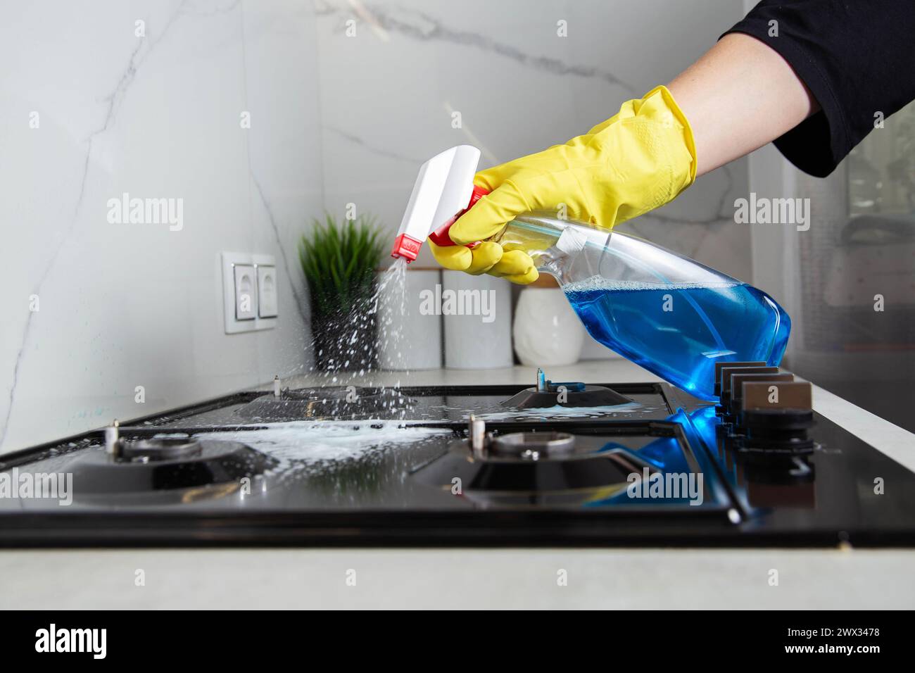 A girl's hand with a cleaning spray sprays on a built-in gas stove ...