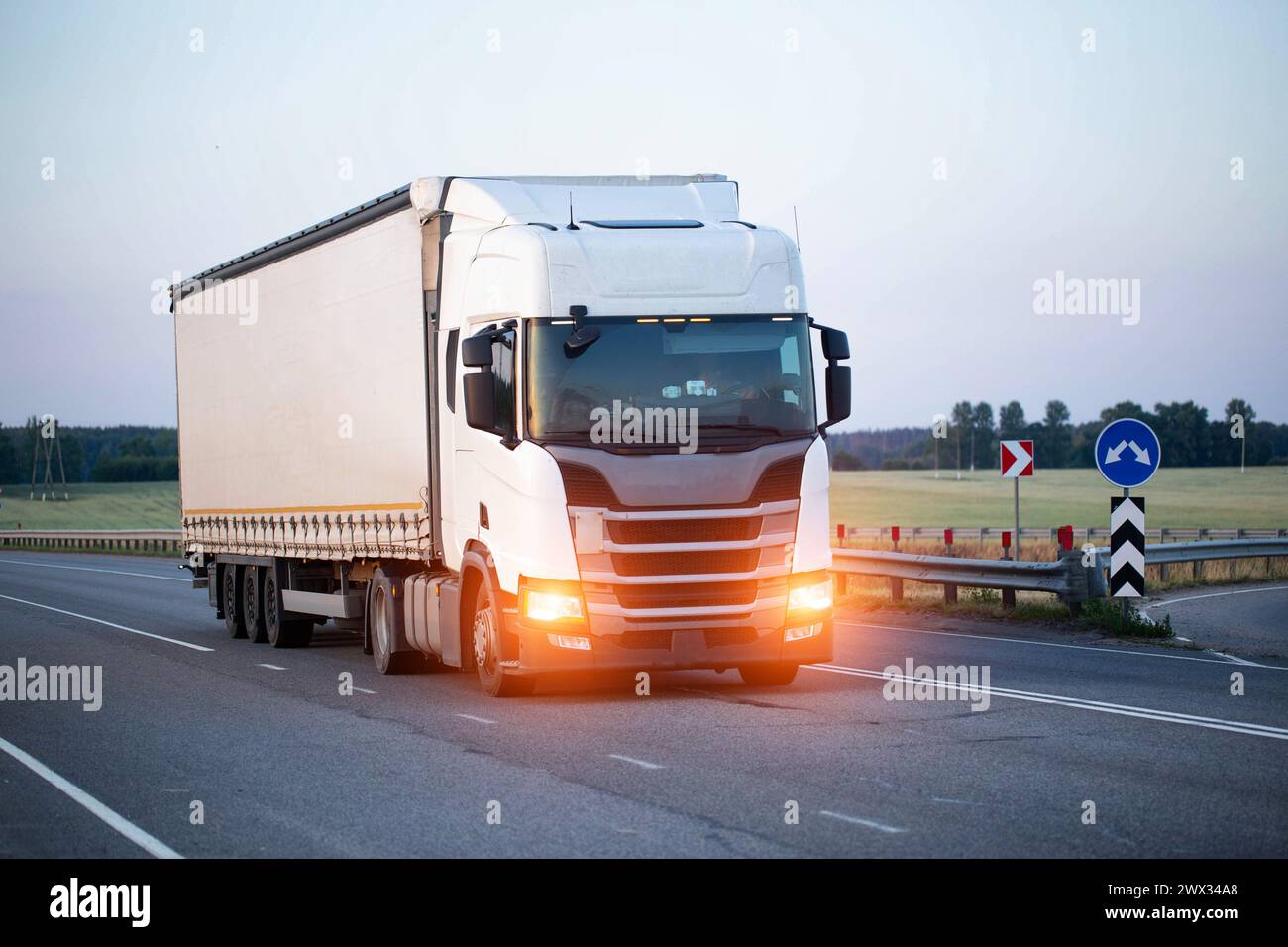 A modern truck with headlights on and a tilted semi-trailer transports ...