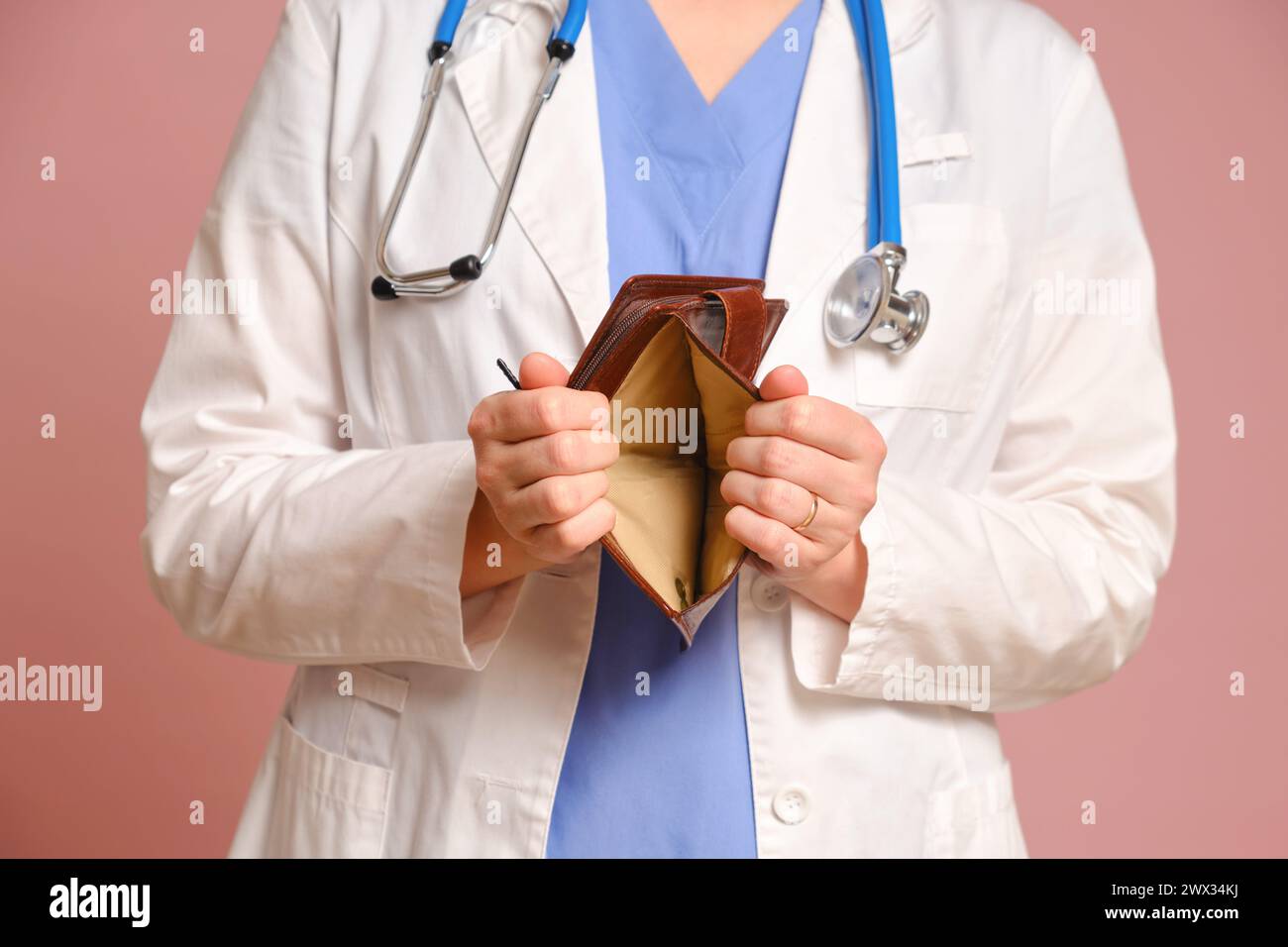 Woman doctor holding an empty wallet in her hands, studio pink ...