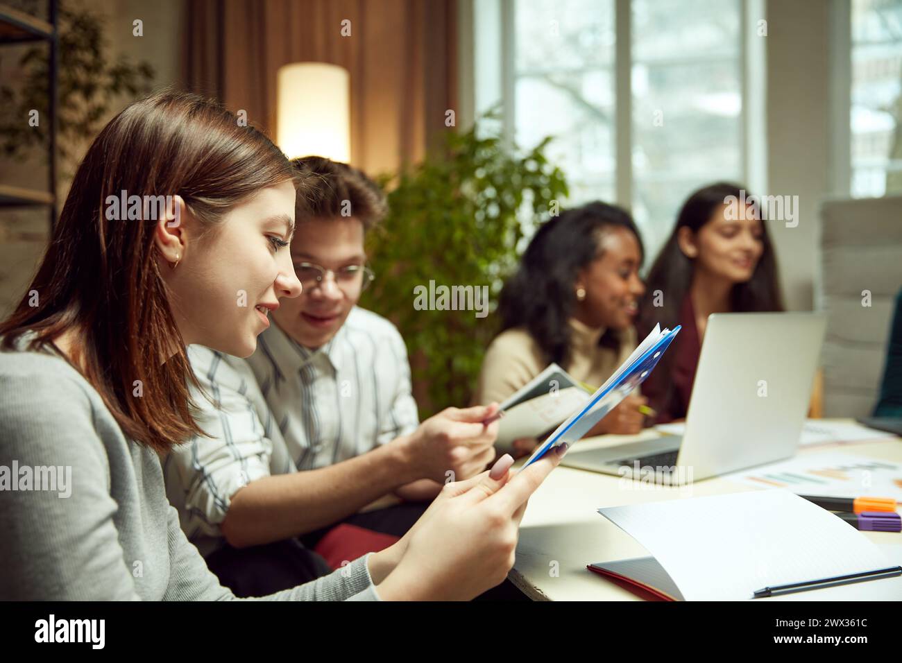 University students sitting together at table with books and laptops ...