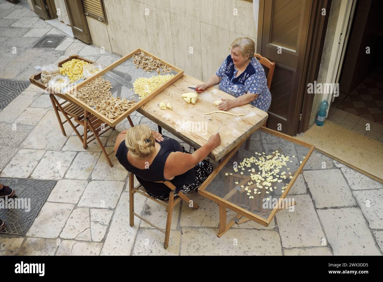 two women making traditional fresh pasta called "orecchiette" in a ...