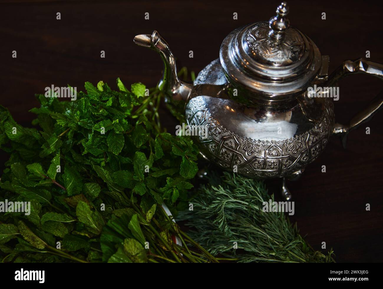 A silver teapot and a bunch of fresh green mint on the foreground ...