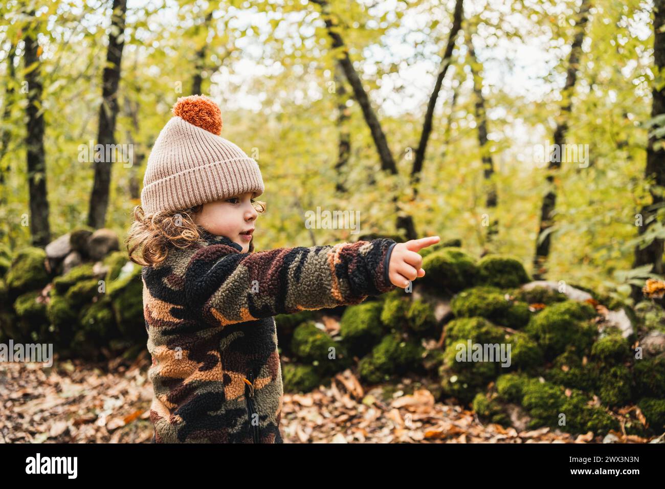 portrait of pretty fashionable little boy with hat in a forest pointing ...