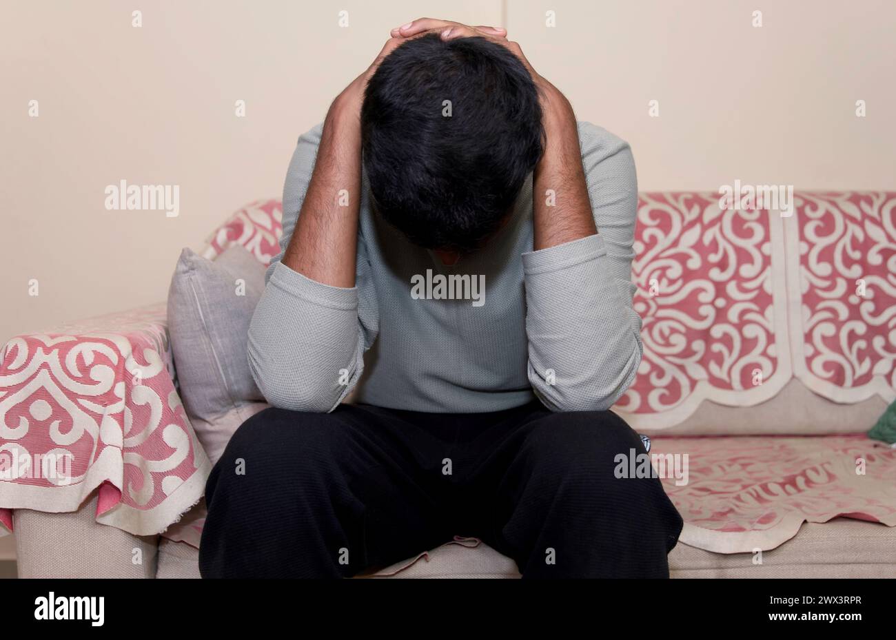 A man slumps on a sofa, his head cradled in his hands, conveying dejection and emotional ...