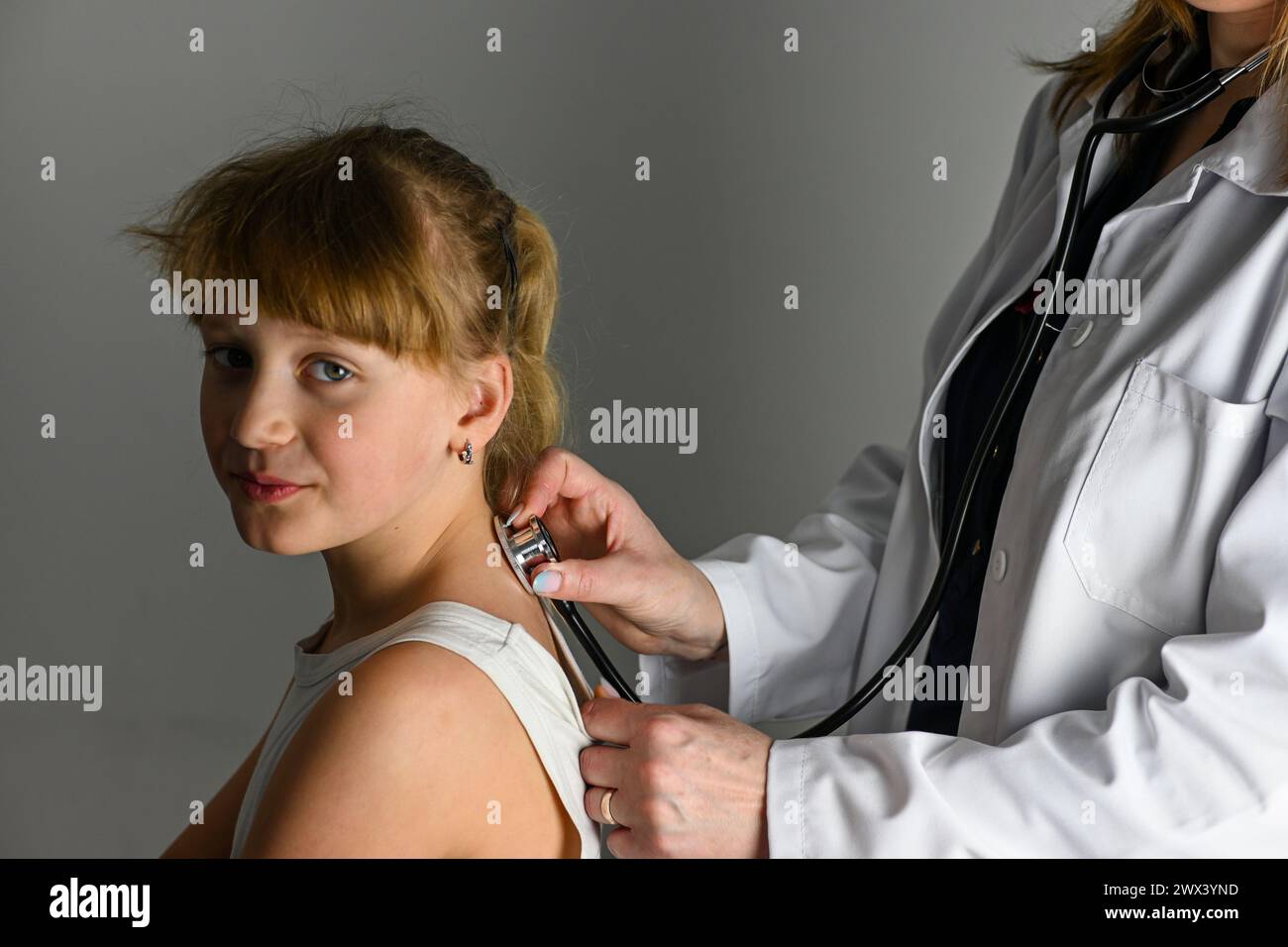 a doctor in a white coat with a stethoscope listens to the little girl ...