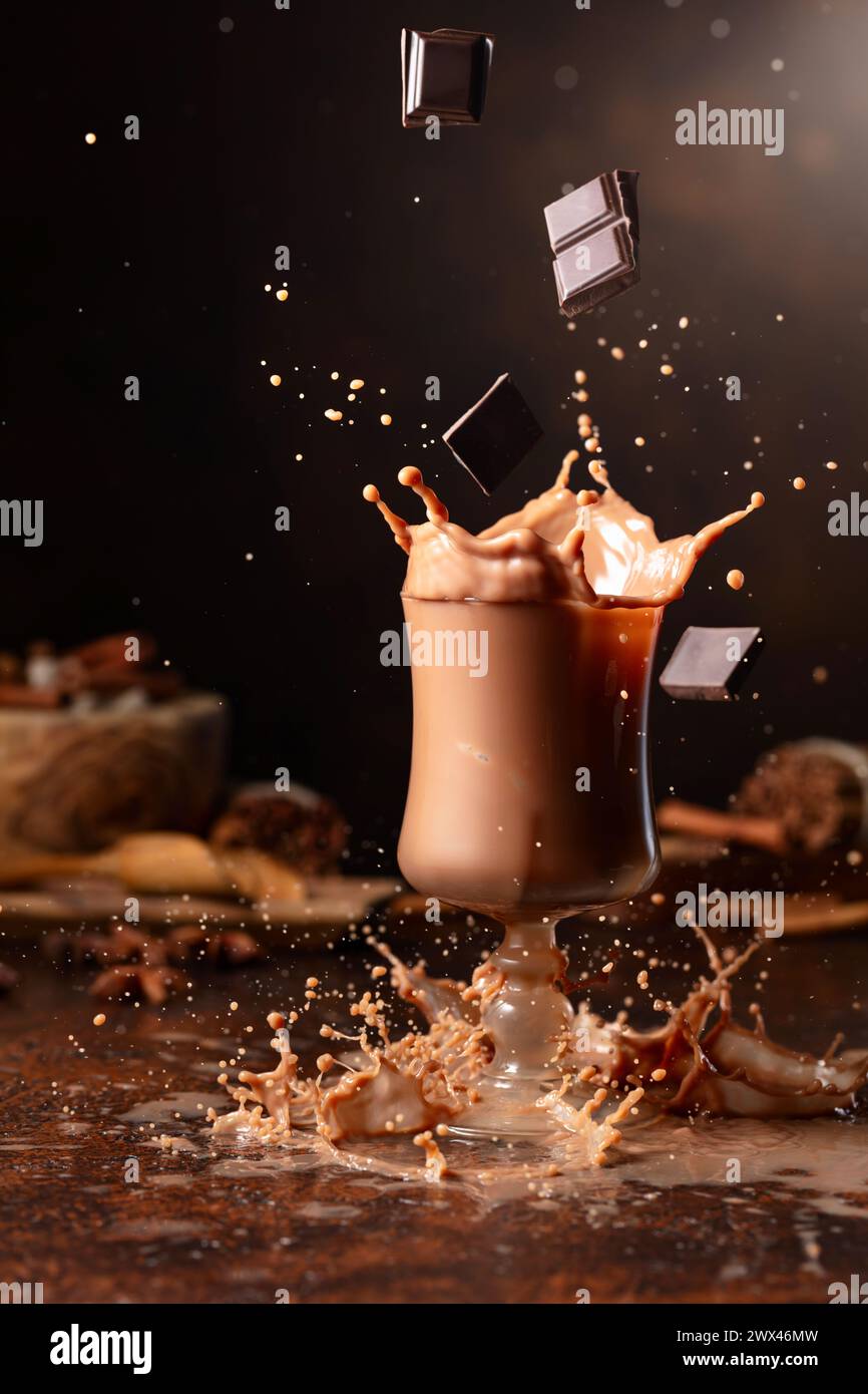 Pieces of dark chocolate fall into a glass of cocoa drink creating a ...