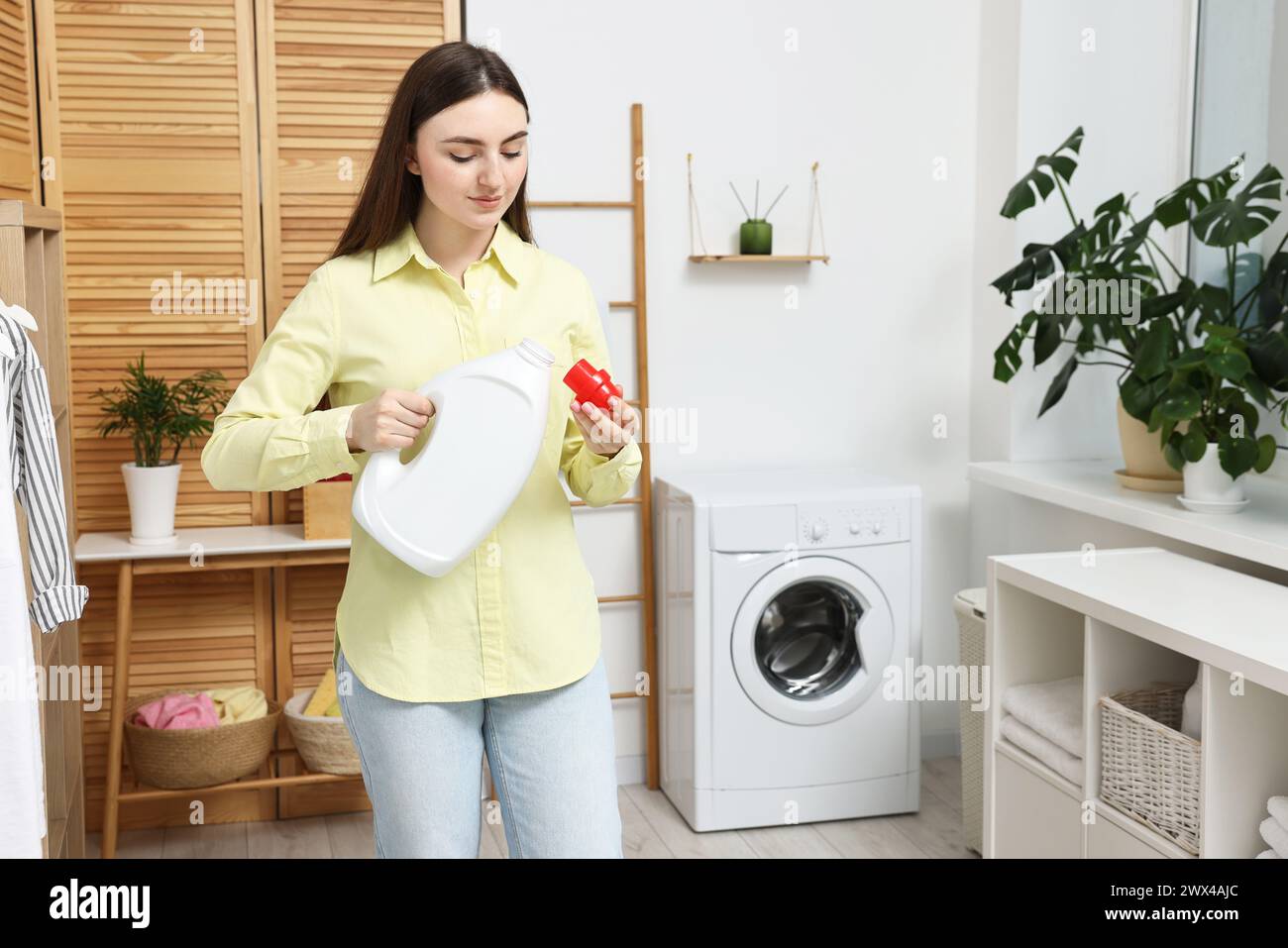 Beautiful young woman pouring detergent into cap in laundry room Stock ...