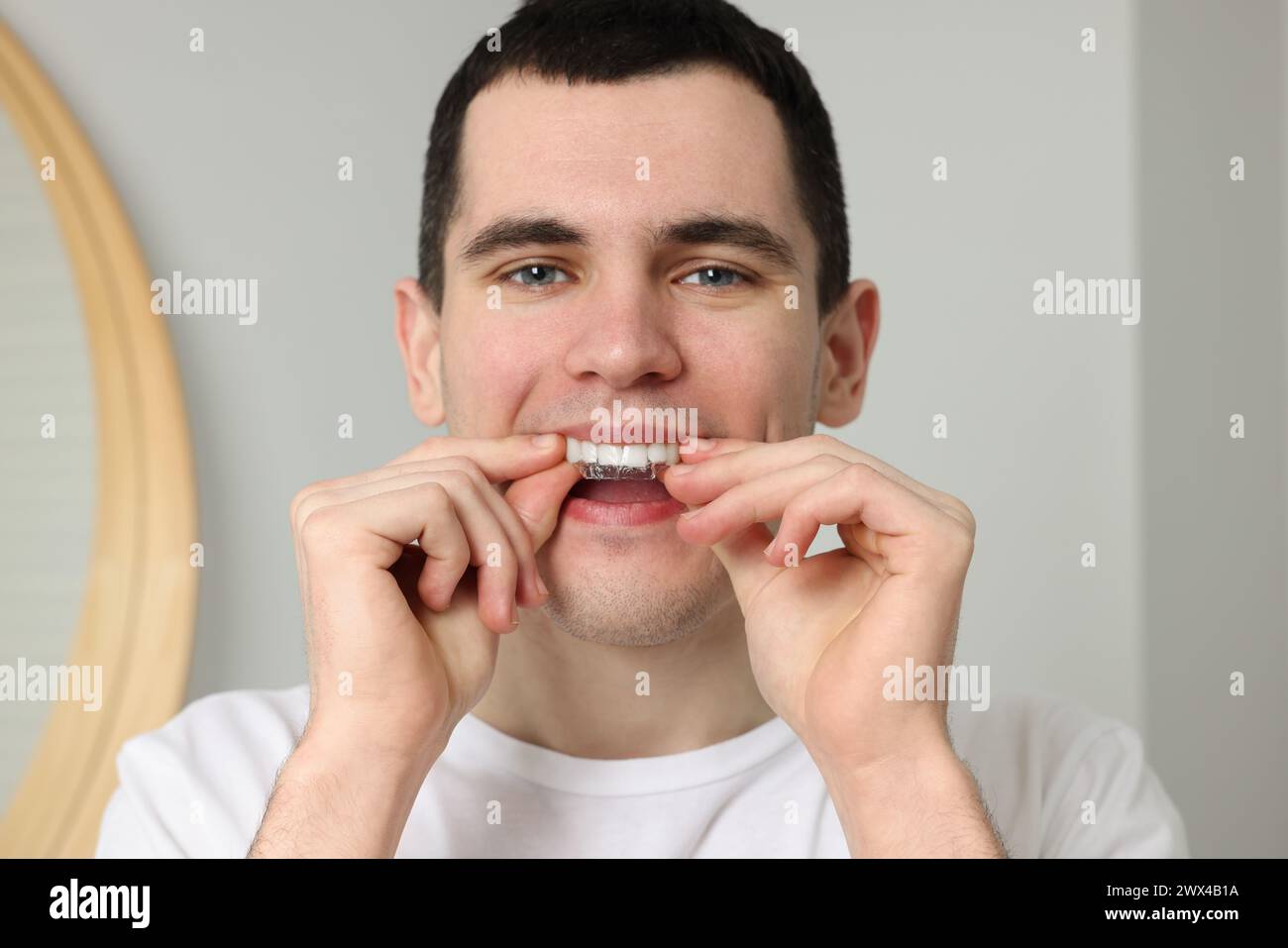 Young man applying whitening strip on his teeth indoors Stock Photo - Alamy