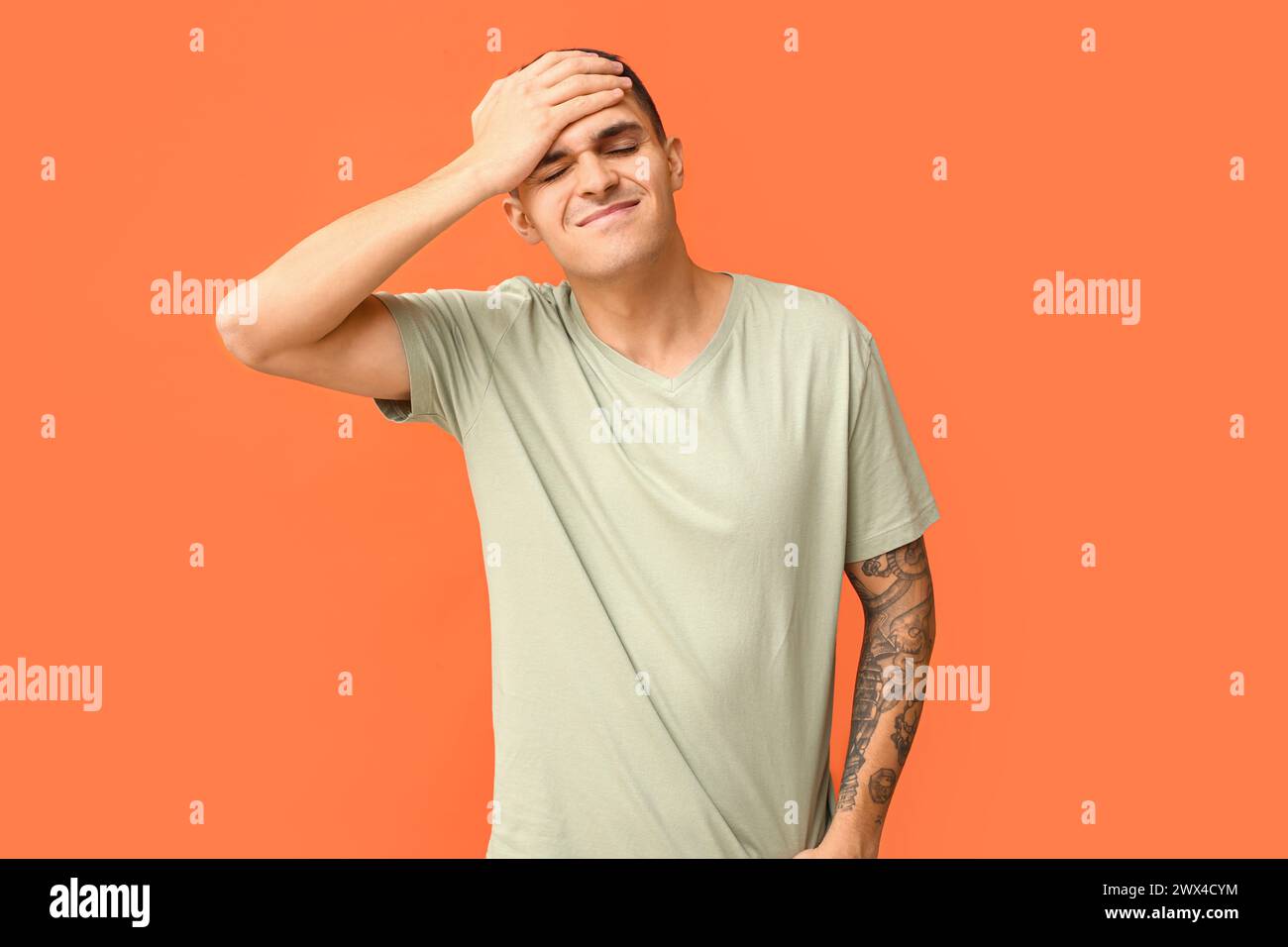 Handsome ashamed young man covering face with hand on orange background ...