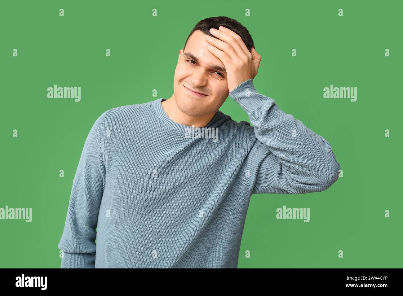 Handsome ashamed young man covering face with hand on green background ...