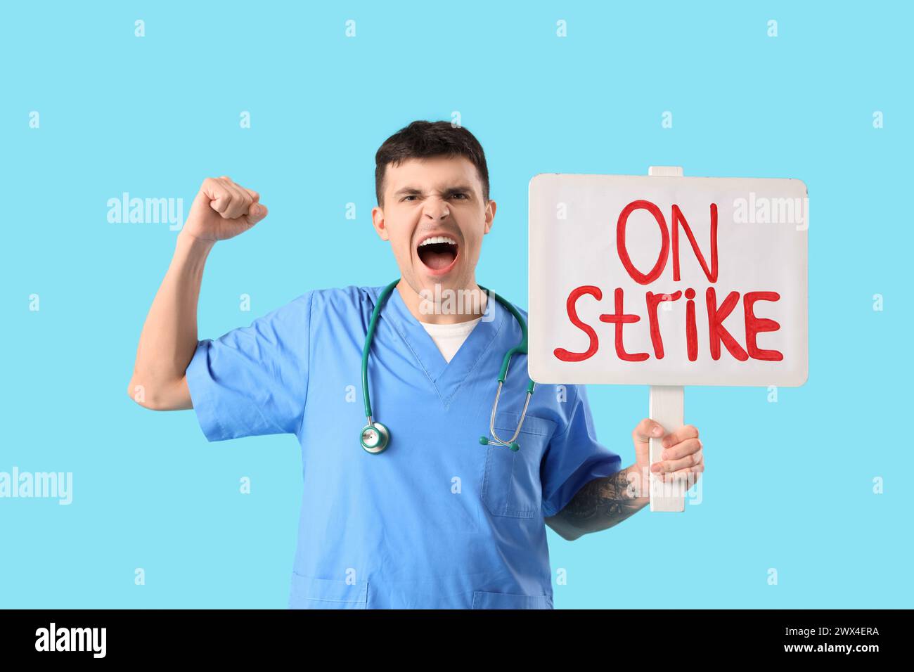 Protesting male doctor holding placard with text ON STRIKE against blue ...