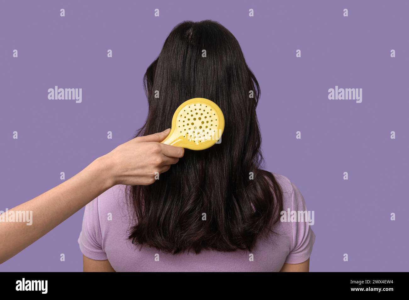 Young woman and hand with hair brush on lilac background, back view ...