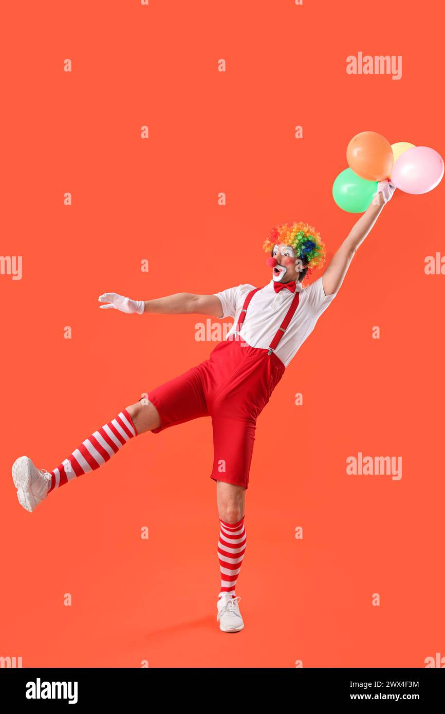 Portrait of surprised clown with balloons on orange background. April ...